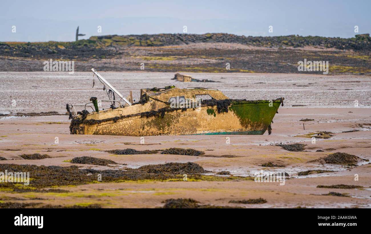 A damaged boat in the mud of the Walney Channel, seen from the road to ...