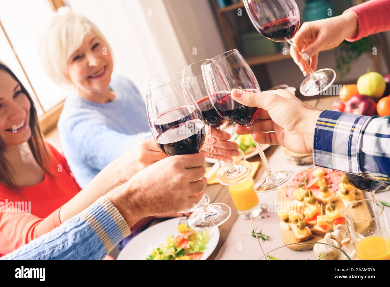 Happy people sitting at home behind table, clinking beverage glasses ...