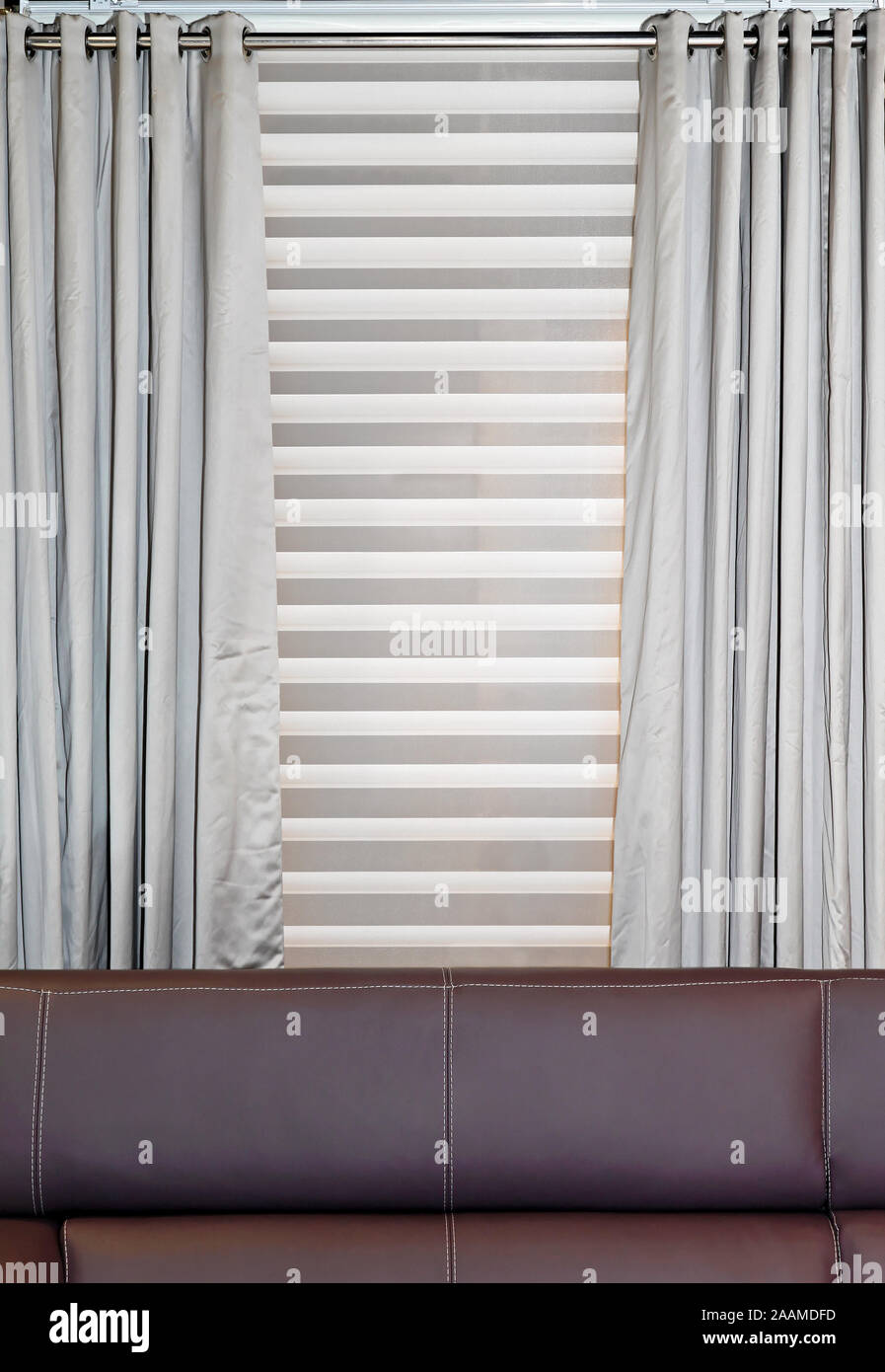 Decorative silver drapes behind brown leather couch Stock Photo - Alamy