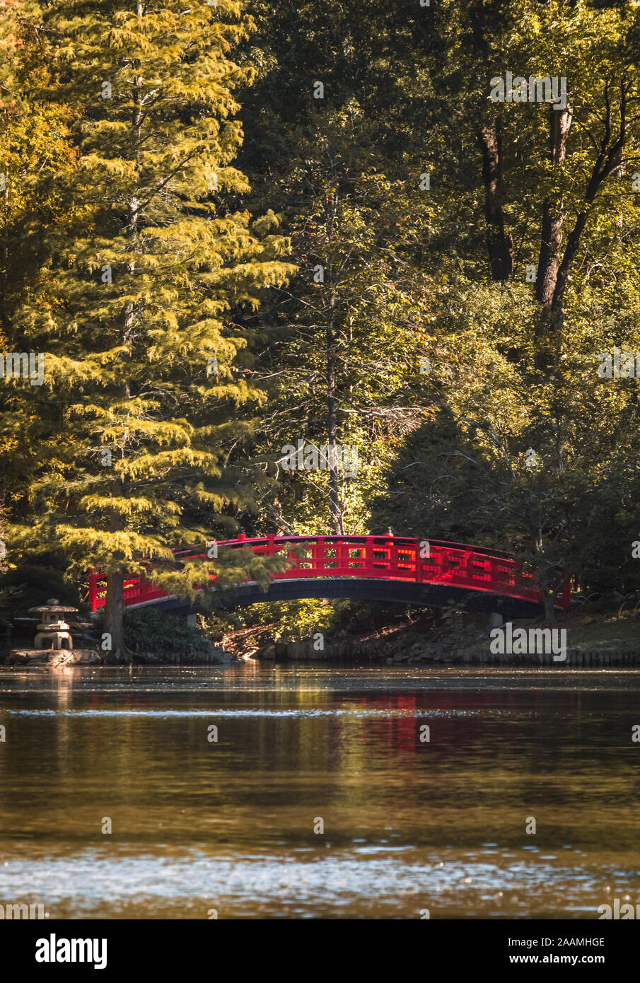 View of a red japanese bridge over a lagoon surrounded by trees on a ...