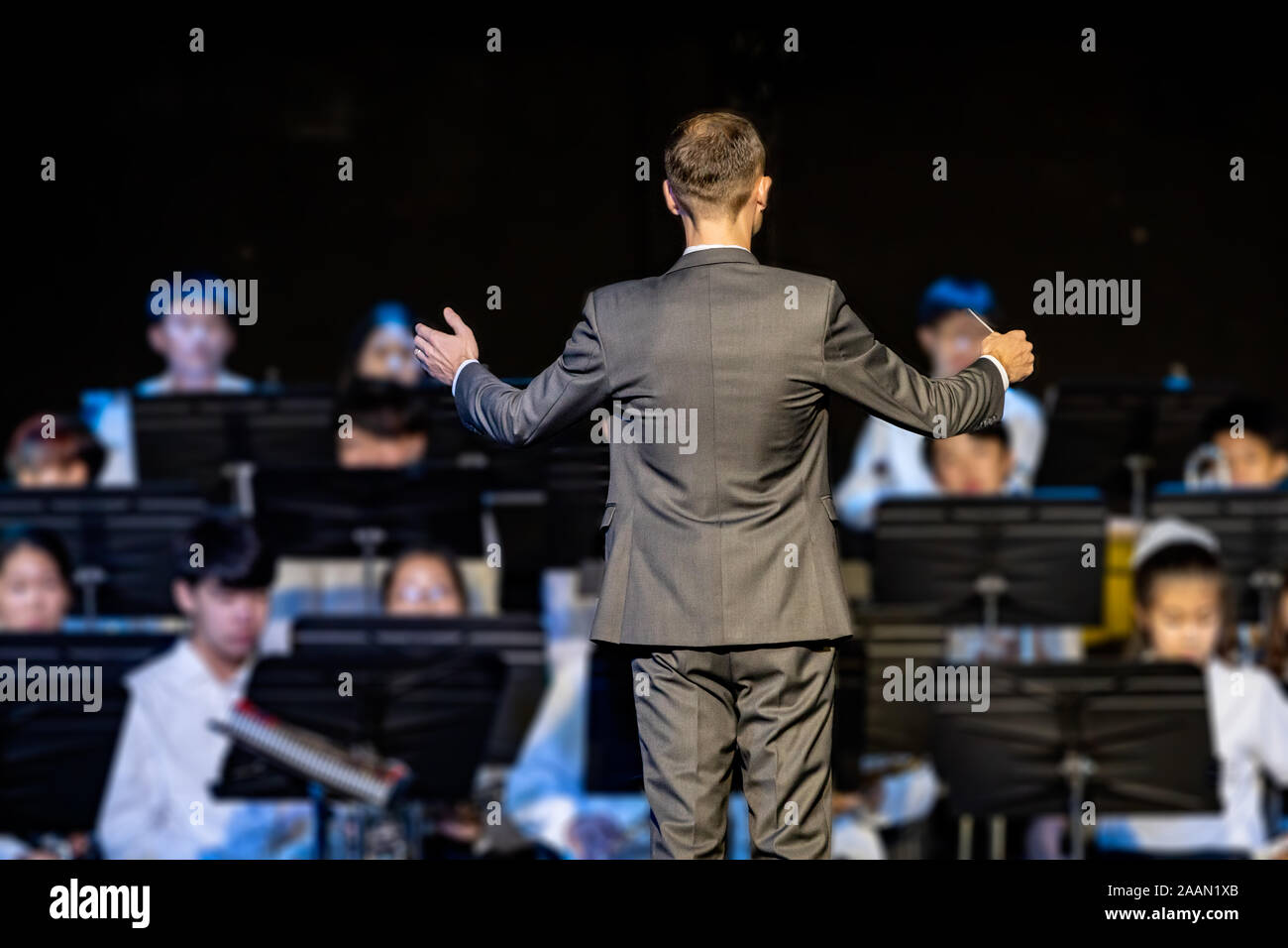 Back view of a male band conductor in formal suit conducting his ...