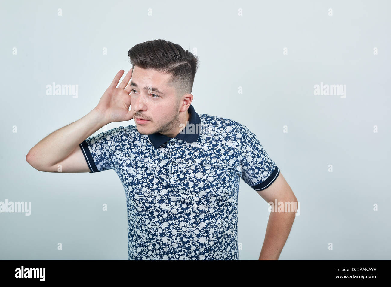 Dashing guy trying to listen something important by putting hands on ...