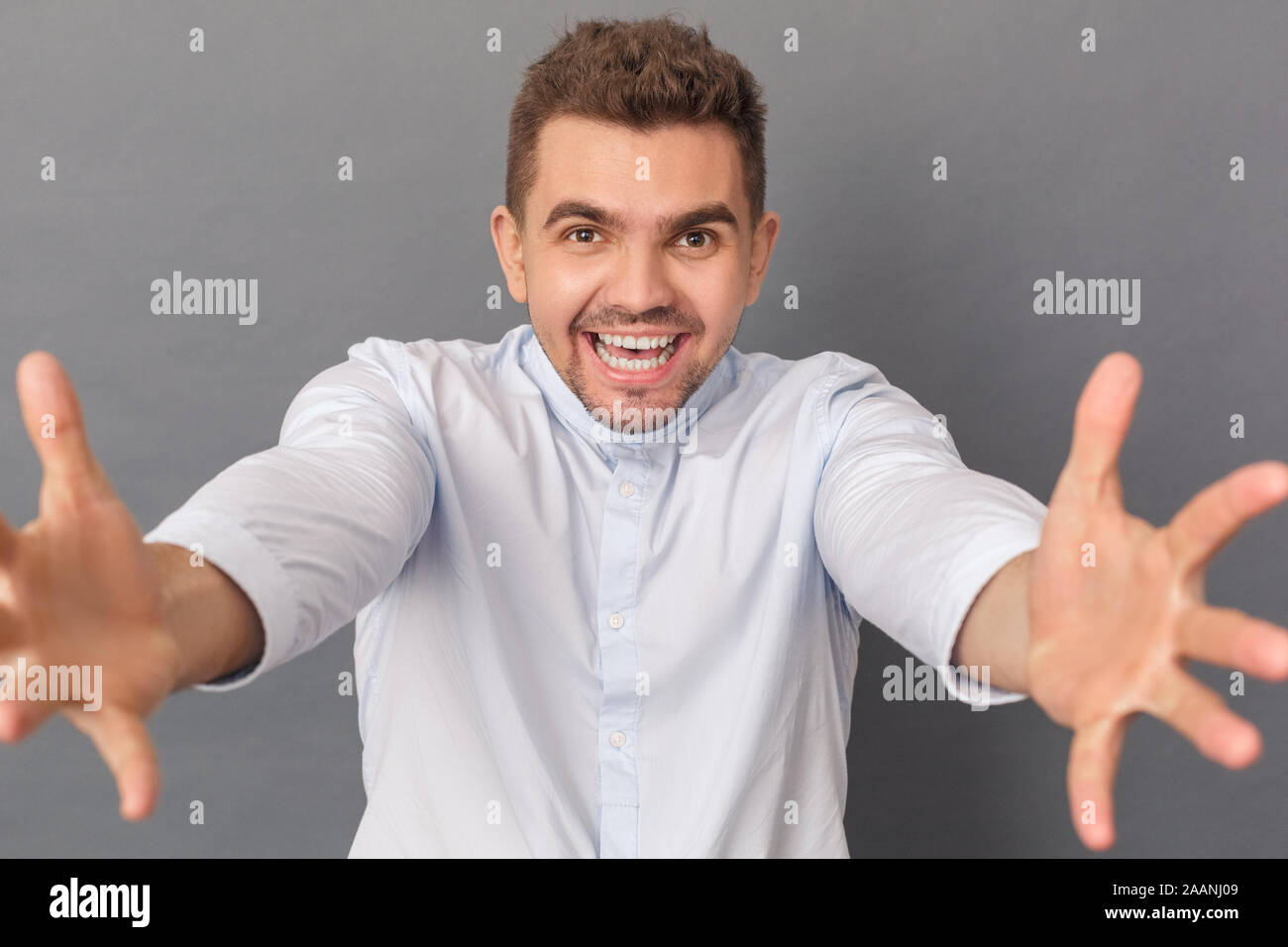 Freestyle. Young man studio standing isolated on grey greeting camera ...