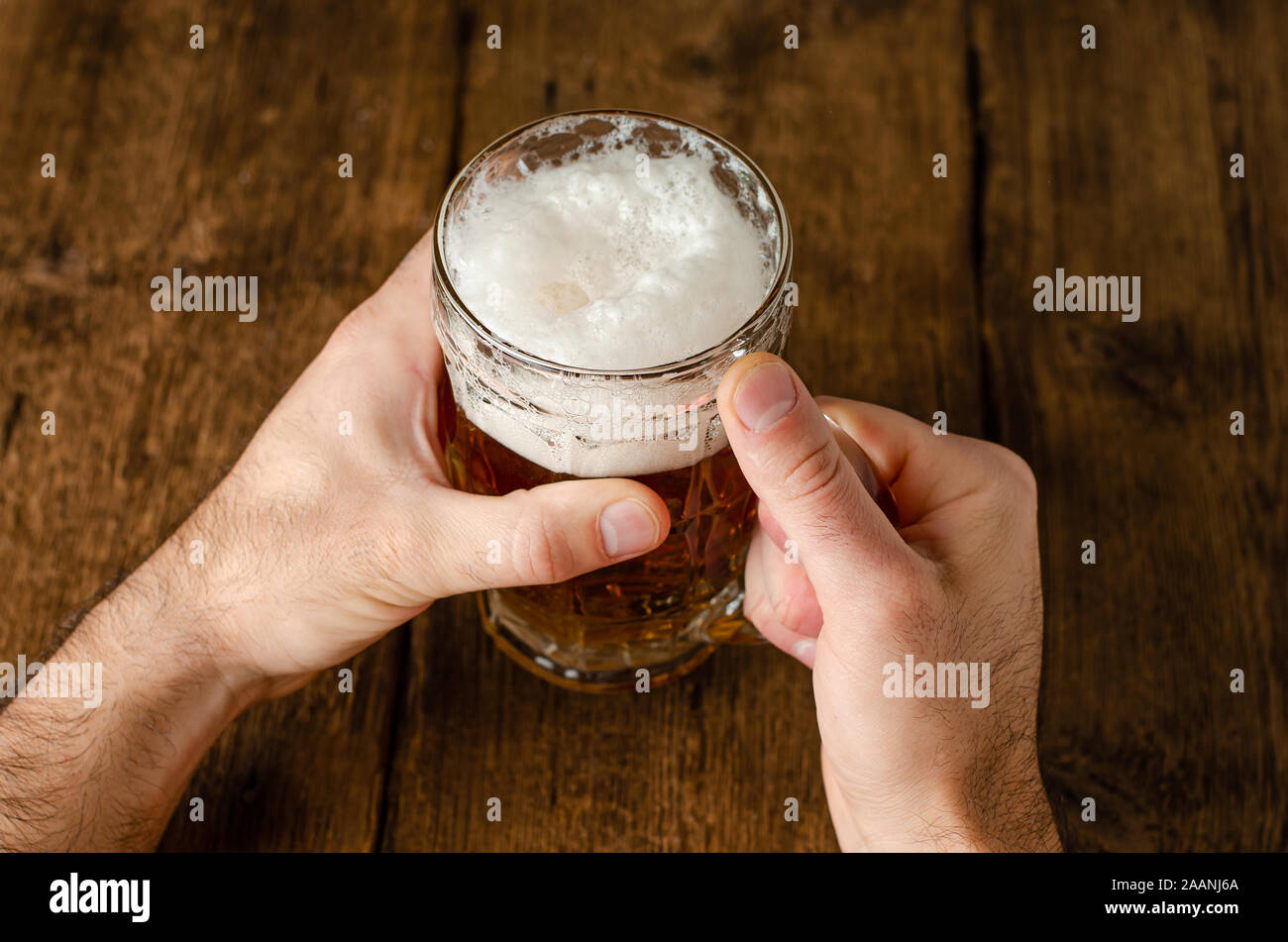 Man's hands holding glass of beer on dark wooden background. Alcoholic ...
