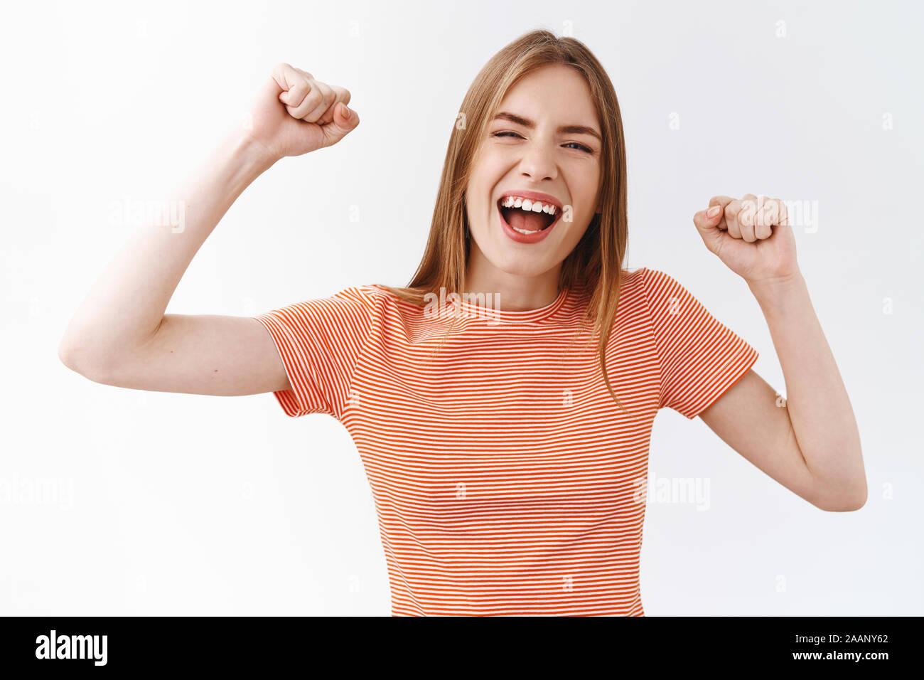 Carefree, happy young lively pretty woman in striped t-shirt, fist pump ...