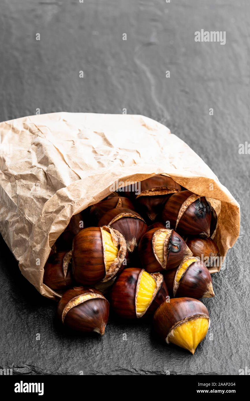 Roasted chestnut scattered of the paper bag on black stone background ...