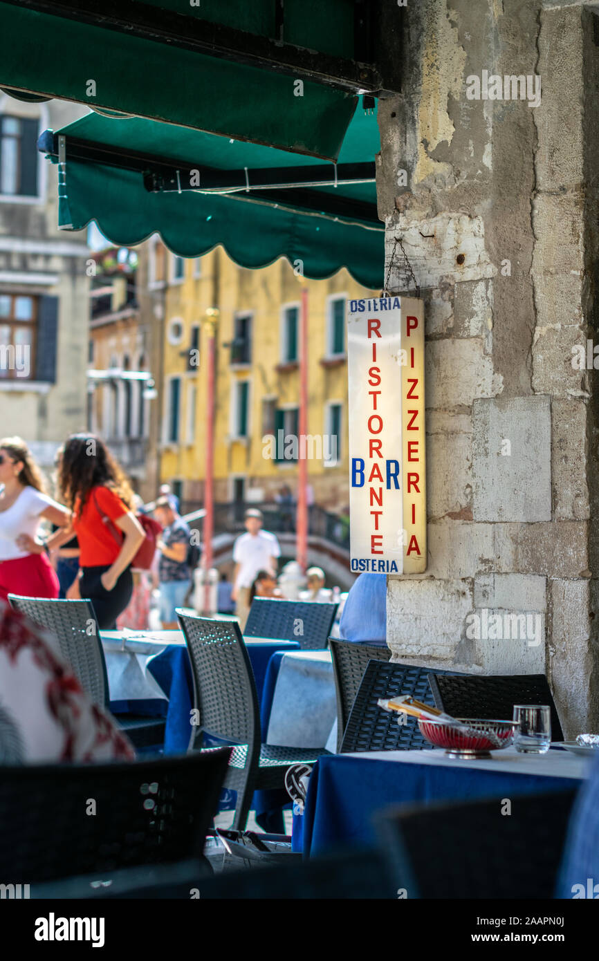 Outdoor tables at a restaurant with an illuminated sign with the words ...
