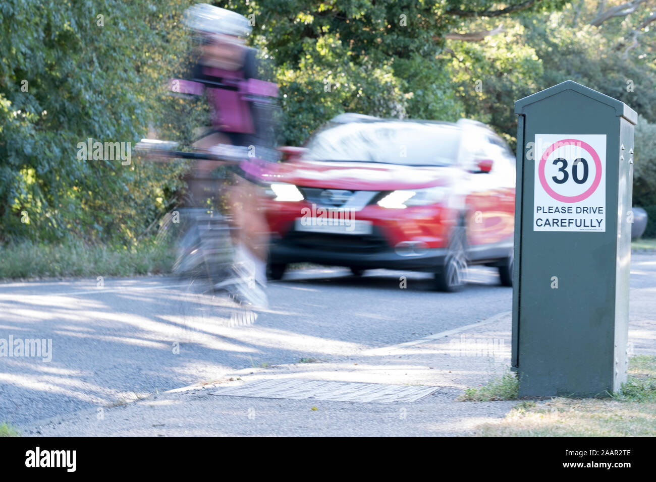 A 30MPH sign as a car and a cyclist go past Stock Photo - Alamy