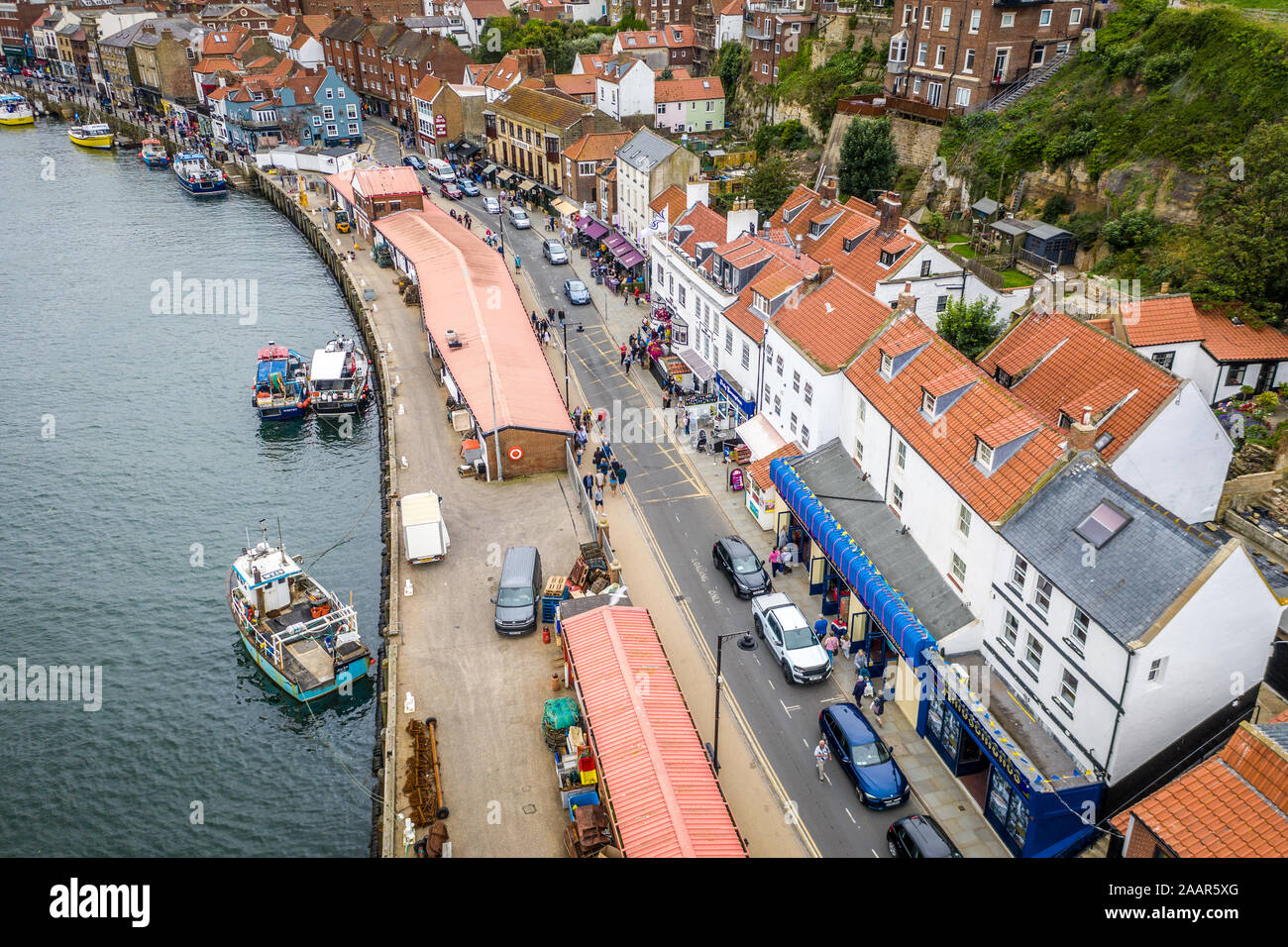 Cars and pedestrians alike travel past the docked boats in the seaside ...
