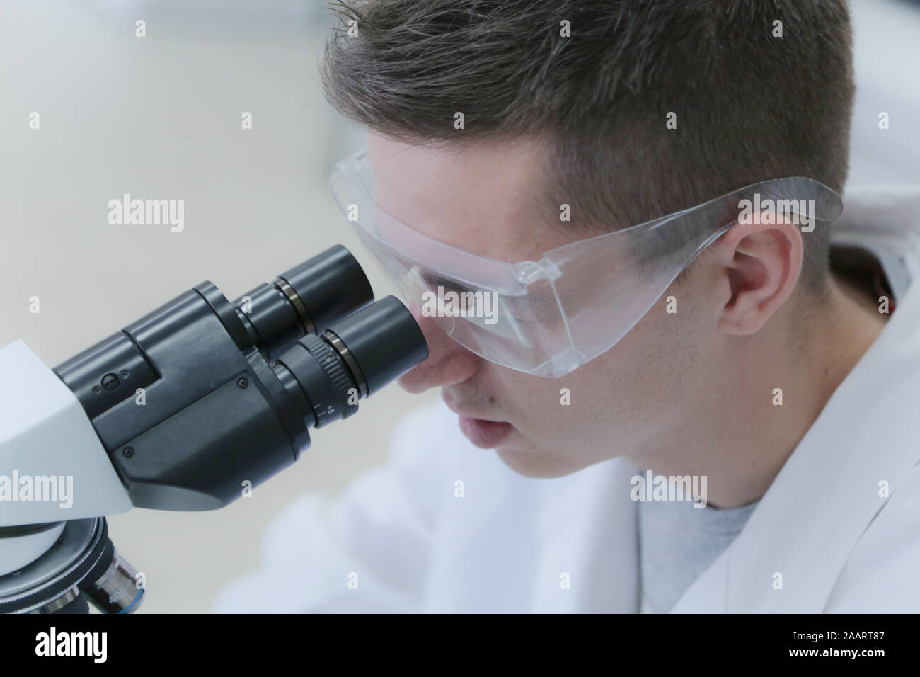 Young male scientist looking through a microscope in a laboratory doing ...