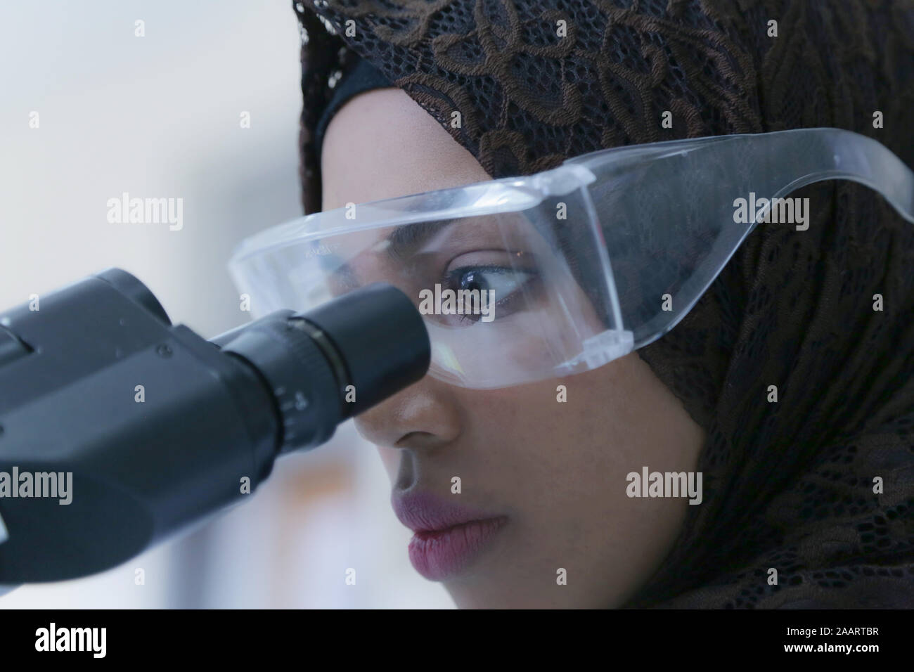 Young african muslim female scientist looking through a microscope in a ...