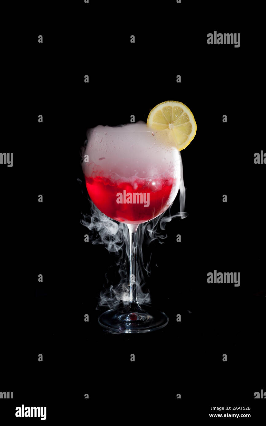 A cup of red cold cocktail with dry ice smoke and a lemon slice and ...