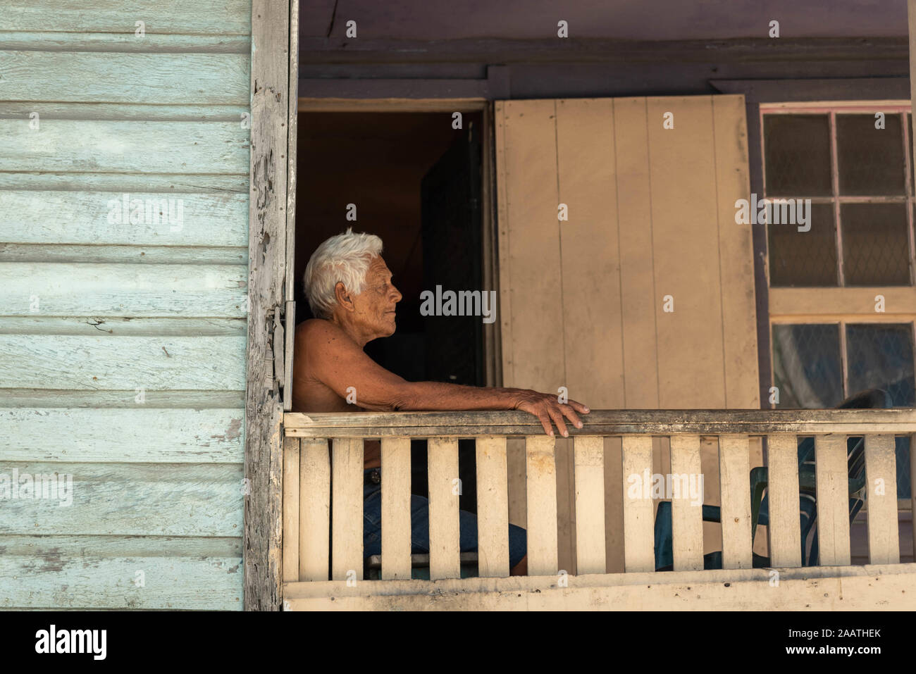 An elderly shirtless, gray haired, Belizean man sitting on the second ...