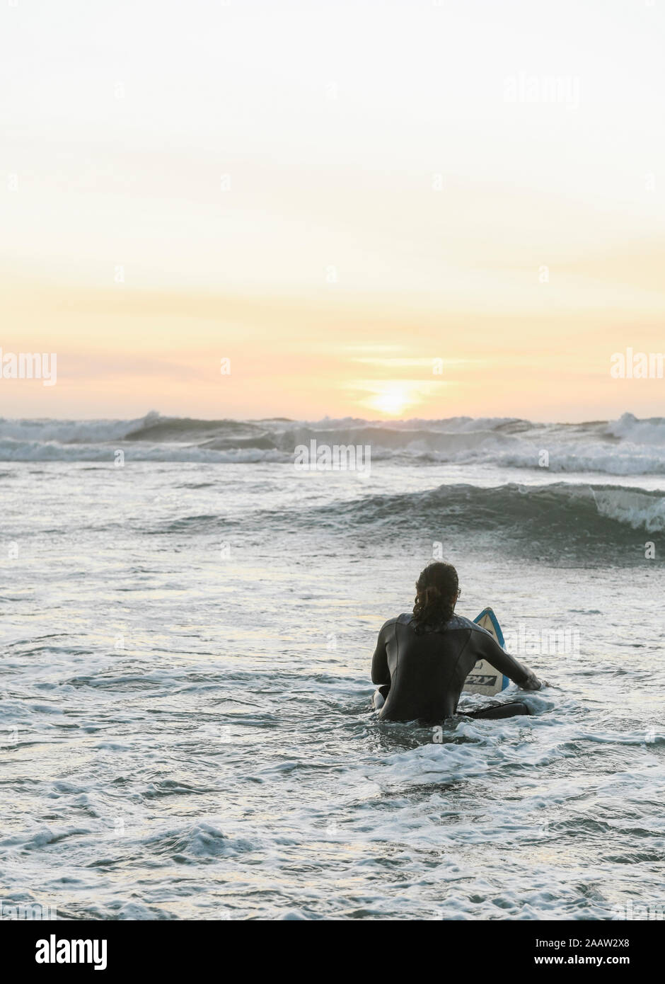 Rear view of surfer with surfboard sitting on surfboard in the ocean ...