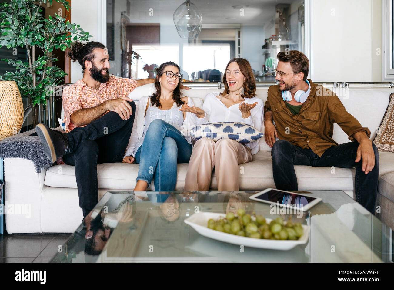 Happy friends sitting on couch together and talking Stock Photo - Alamy