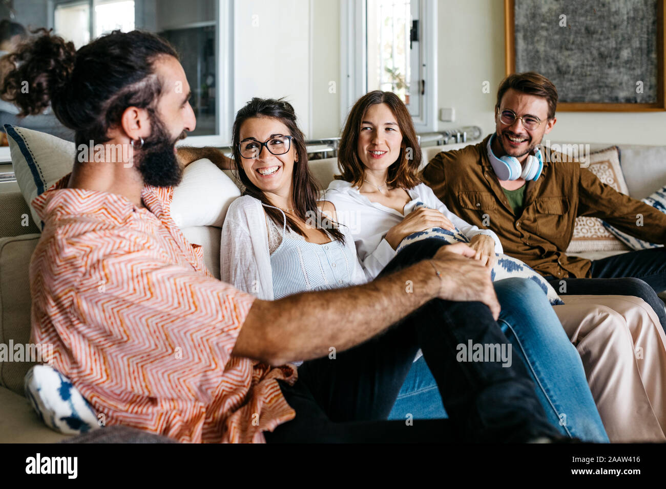 Happy friends sitting on couch together and talking Stock Photo - Alamy
