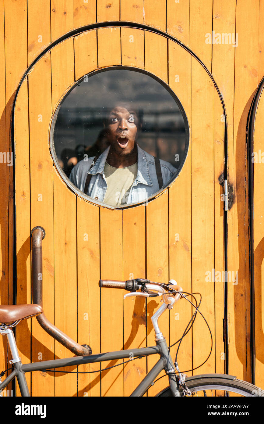 Young man behind wooden door, looking amazed through round window Stock ...