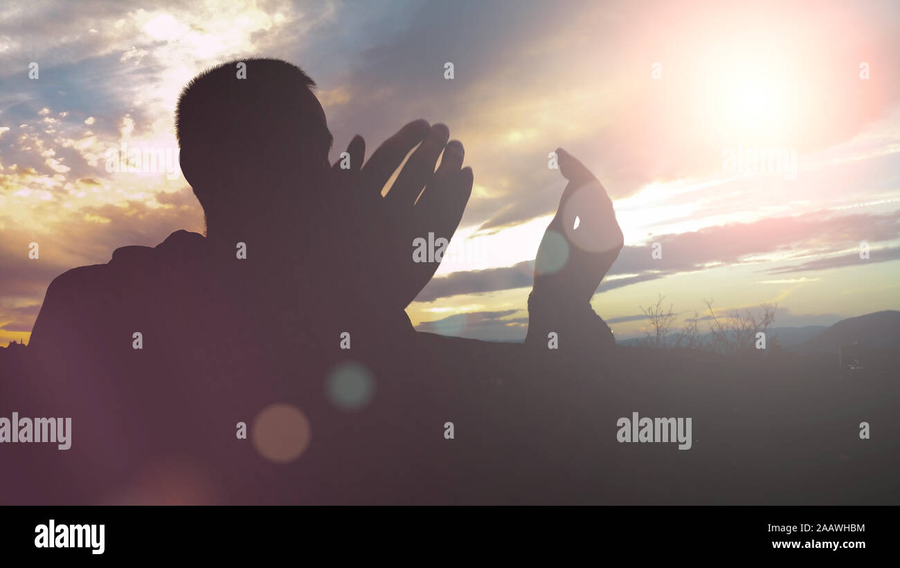 Silhouette of young muslim man praying outside during sunset with lens ...