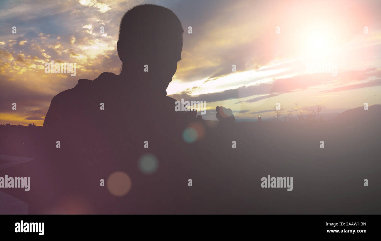 Silhouette of young muslim man praying outside during sunset with lens ...
