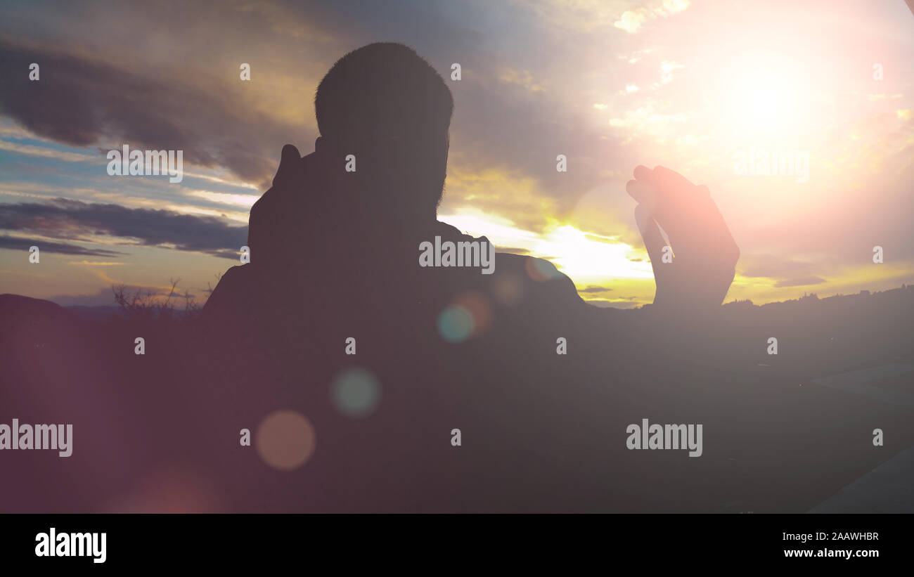 Silhouette of young muslim man praying outside during sunset with lens ...