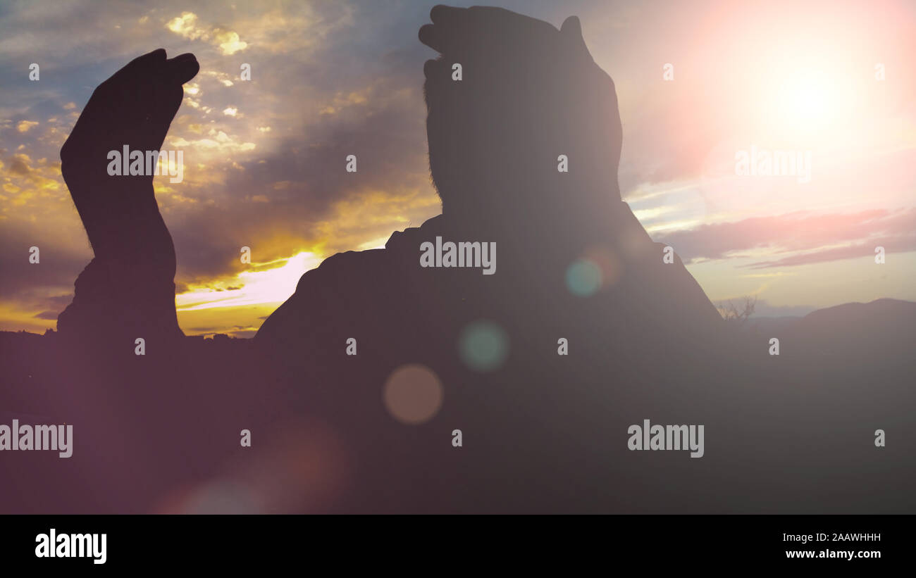 Silhouette of young muslim man praying outside during sunset with lens ...