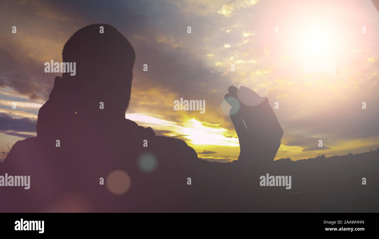 Silhouette of young muslim man praying outside during sunset with lens ...
