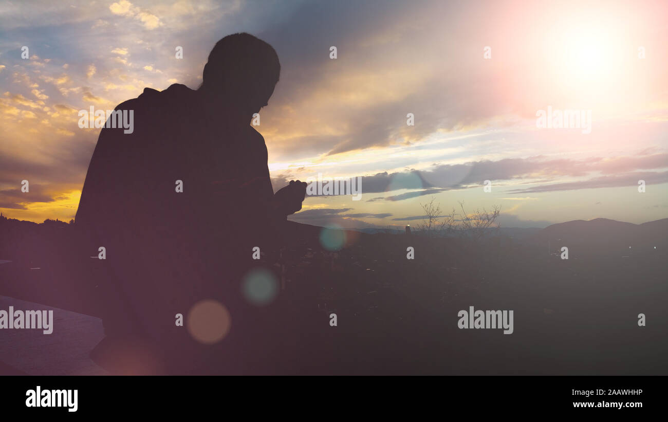 Silhouette of young muslim man praying outside during sunset with lens ...