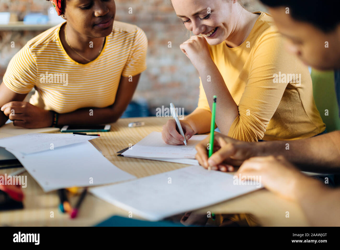 Young people sitting together at table and taking notes Stock Photo - Alamy