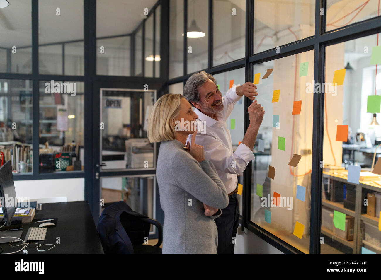Happy colleagues looking at sticky notes at glass pane in office Stock ...