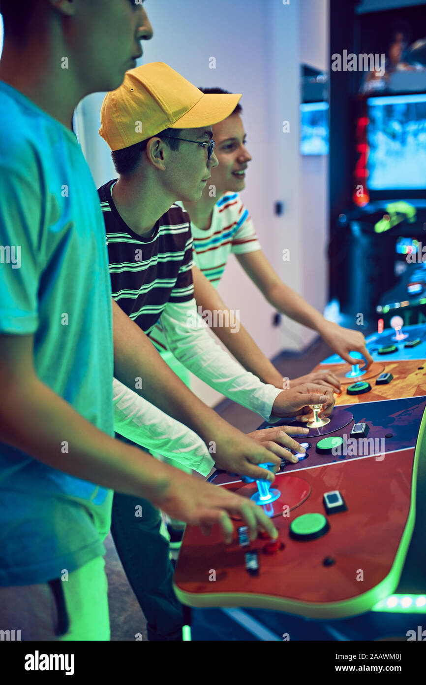 Teenage friends playing with a gaming machine in an amusement arcade ...