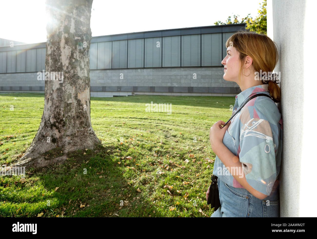 Smiling young woman leaning against wall enjoying sunlight Stock Photo ...