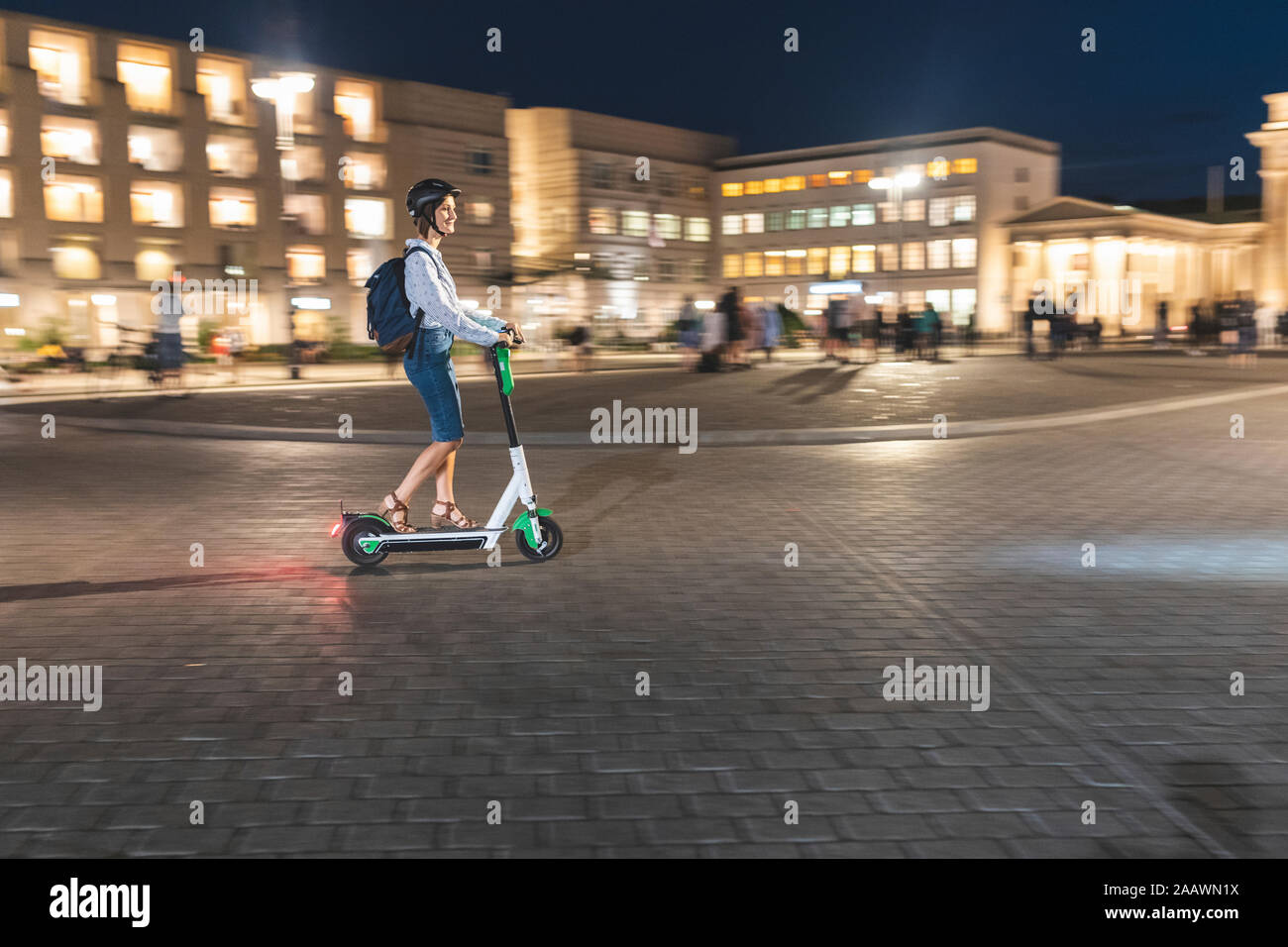 Young woman riding an electric scooter on 'Pariser Platz' at night ...