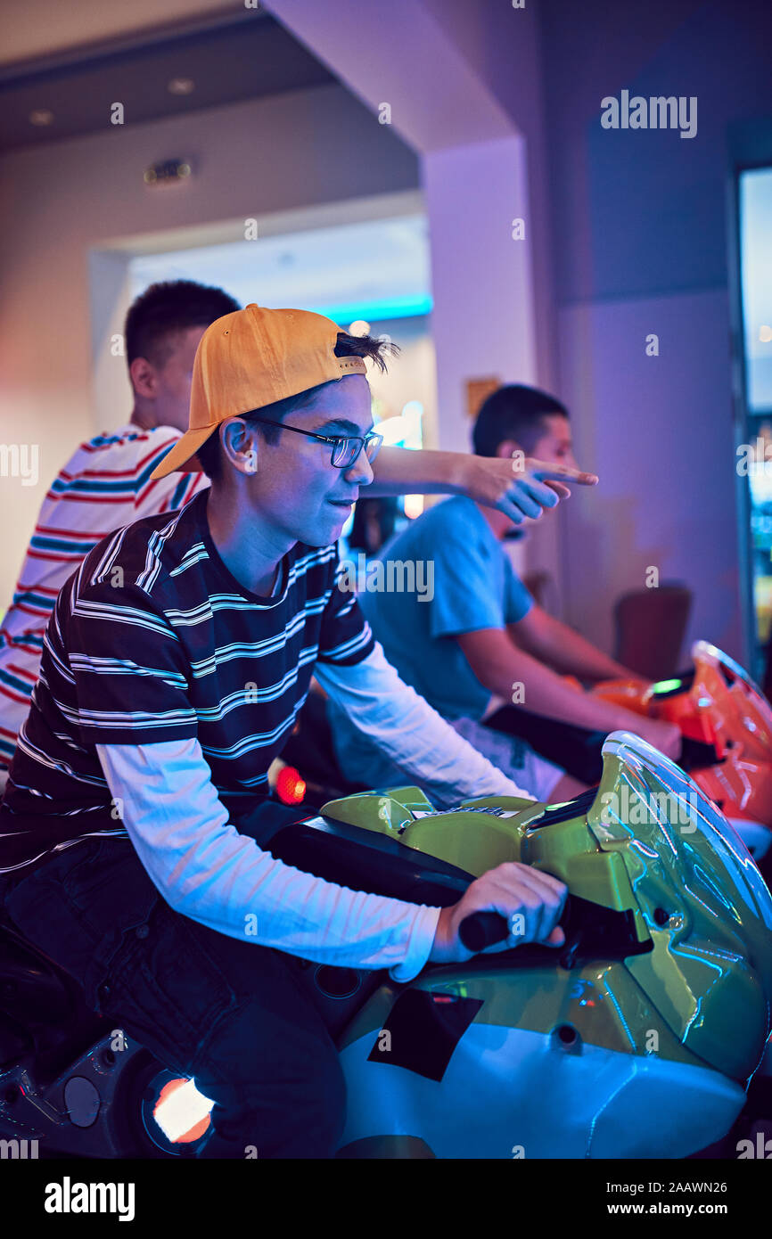Teenage friends playing with a driving simulator in an amusement arcade ...