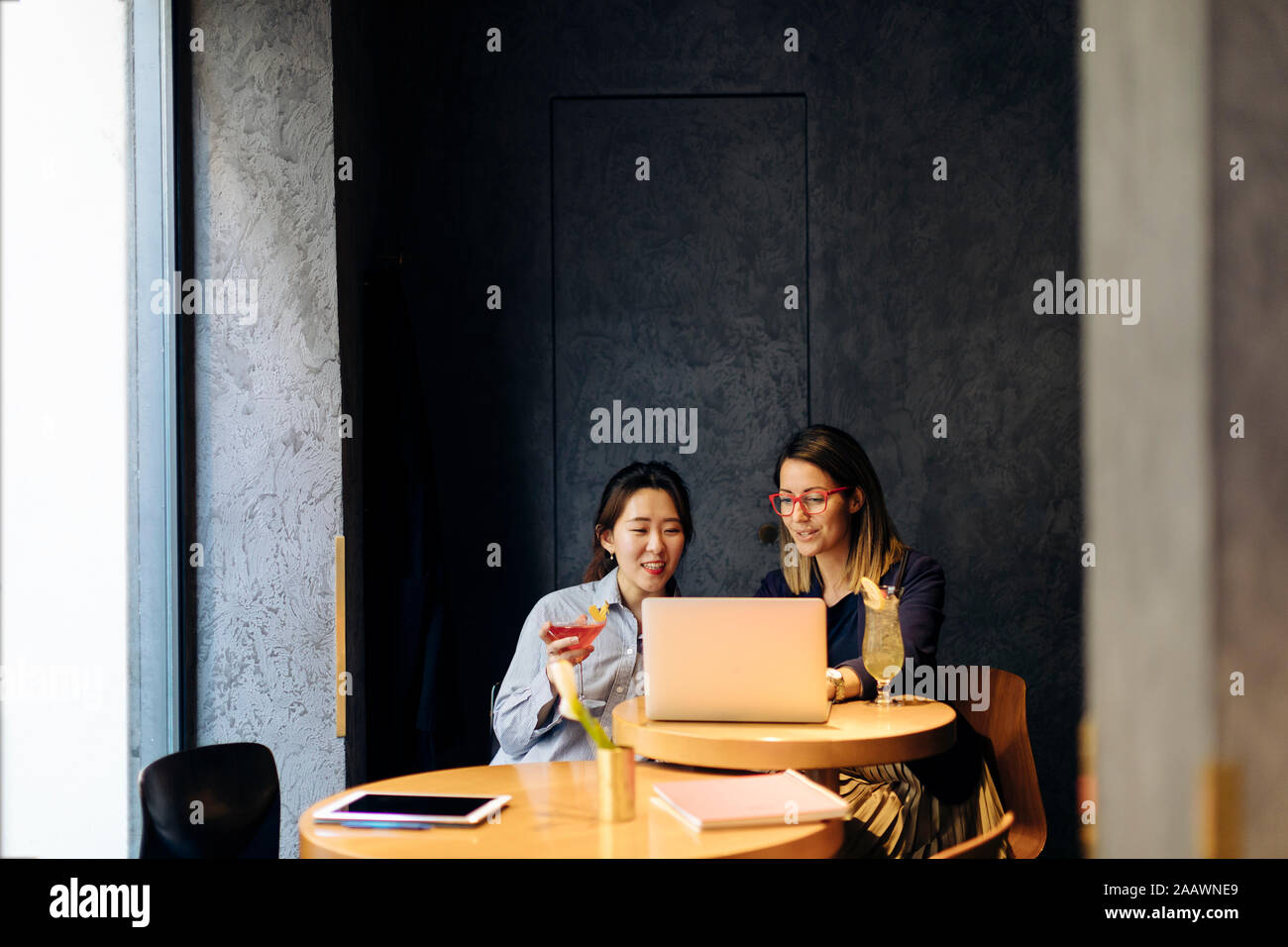 Colleagues discussing work, using laptop, drinking after work cocktails ...
