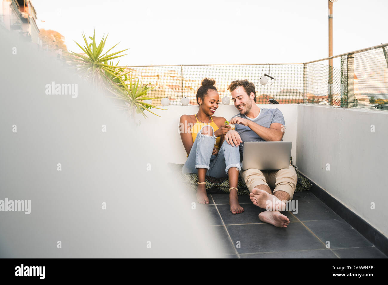 Young couple with laptop sitting on rooftop in the evening Stock Photo ...