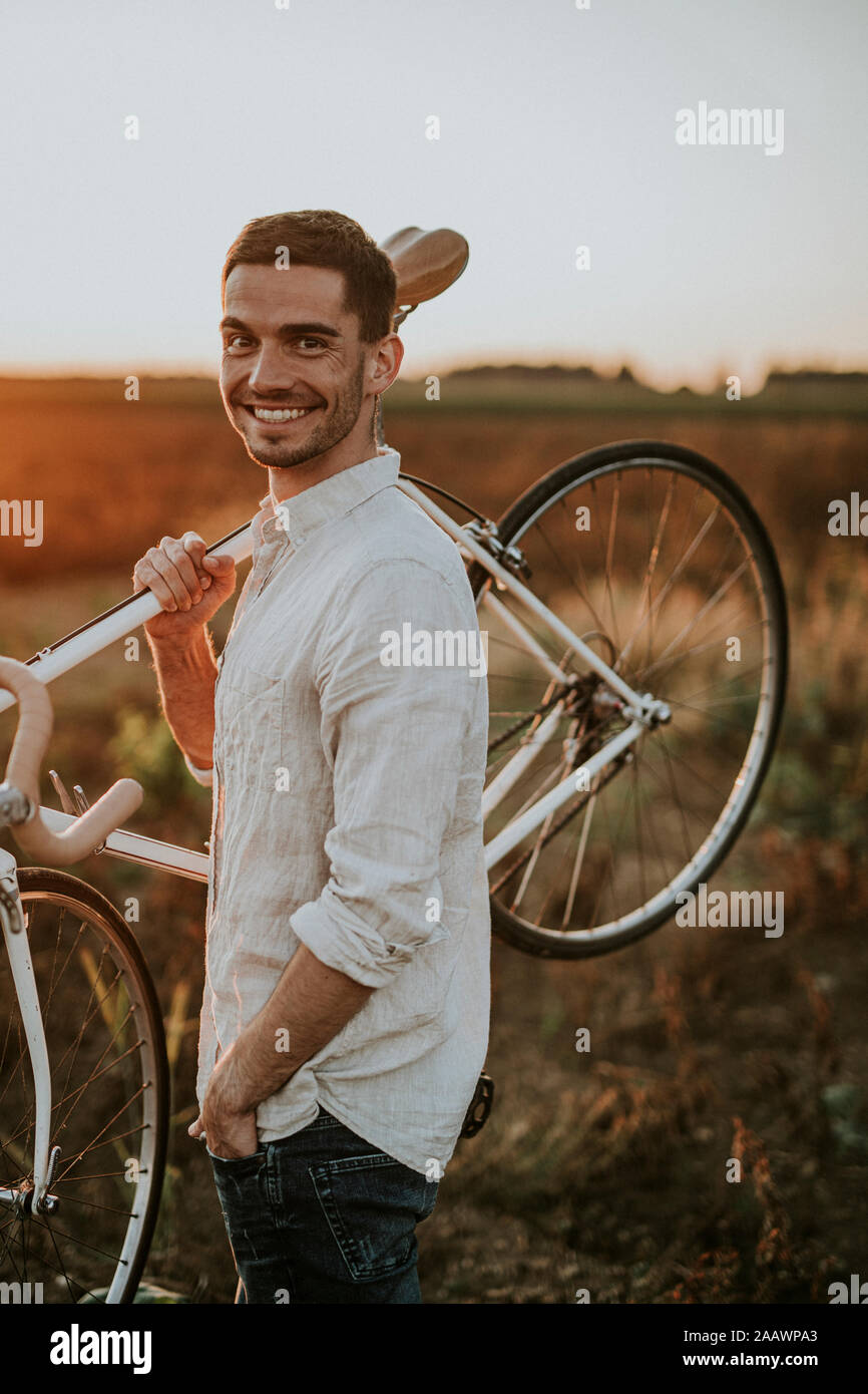Portrait of a smiling young man carrying a racing cycle in the sunshine ...