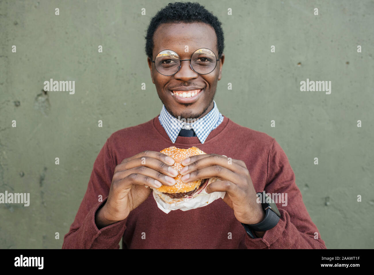Young man eating cheeseburger, smiling Stock Photo - Alamy