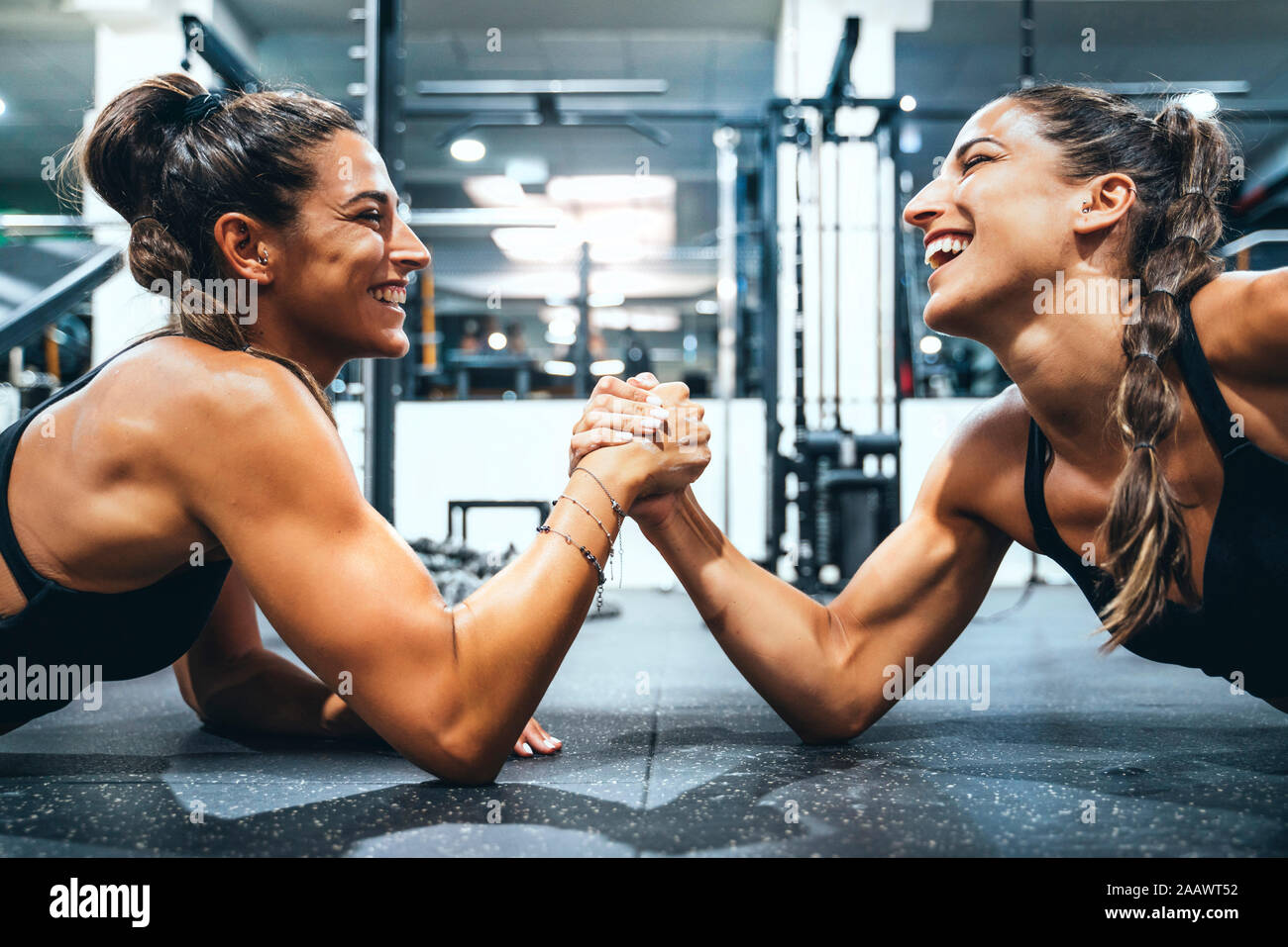 Happy female twins in good shape doing arm wrestling challenge in a gym ...