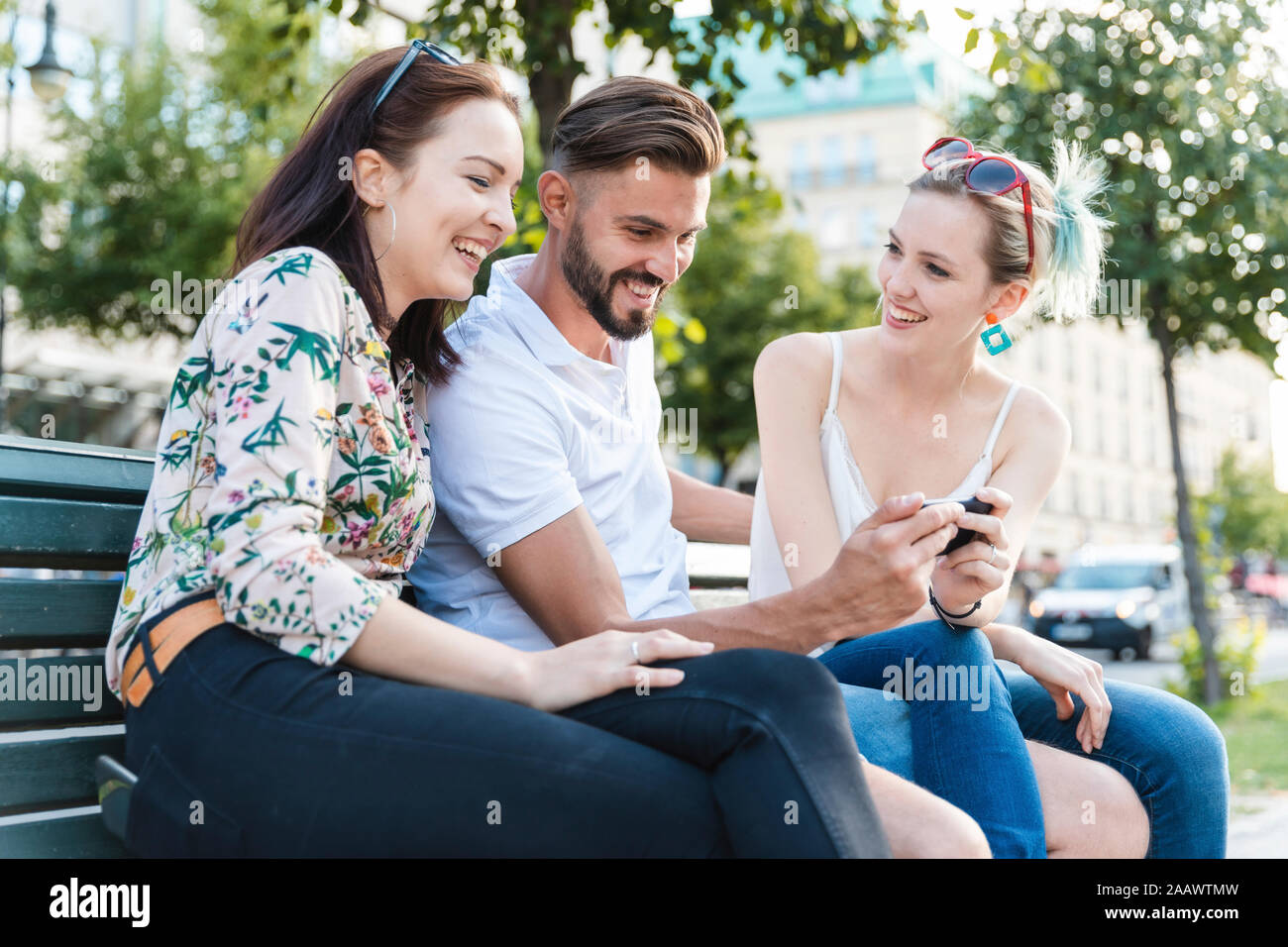 Three friends sitting together on a bench looking at cell phone Stock ...