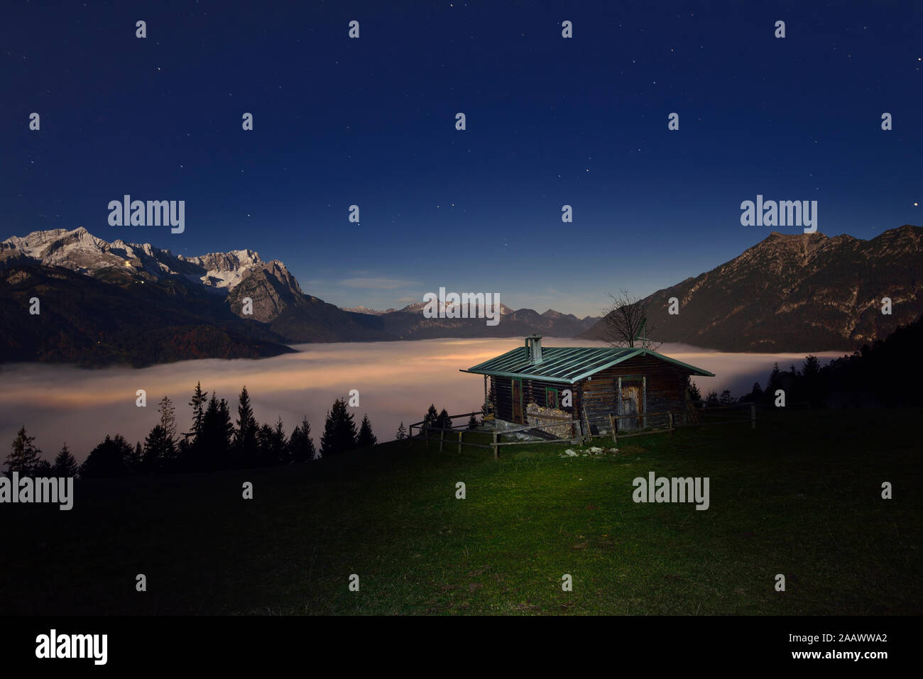 Log cabin at Mt. Wank with beautiful Mount Zugspitze and cloudscape at night, Bavaria, Germany ...