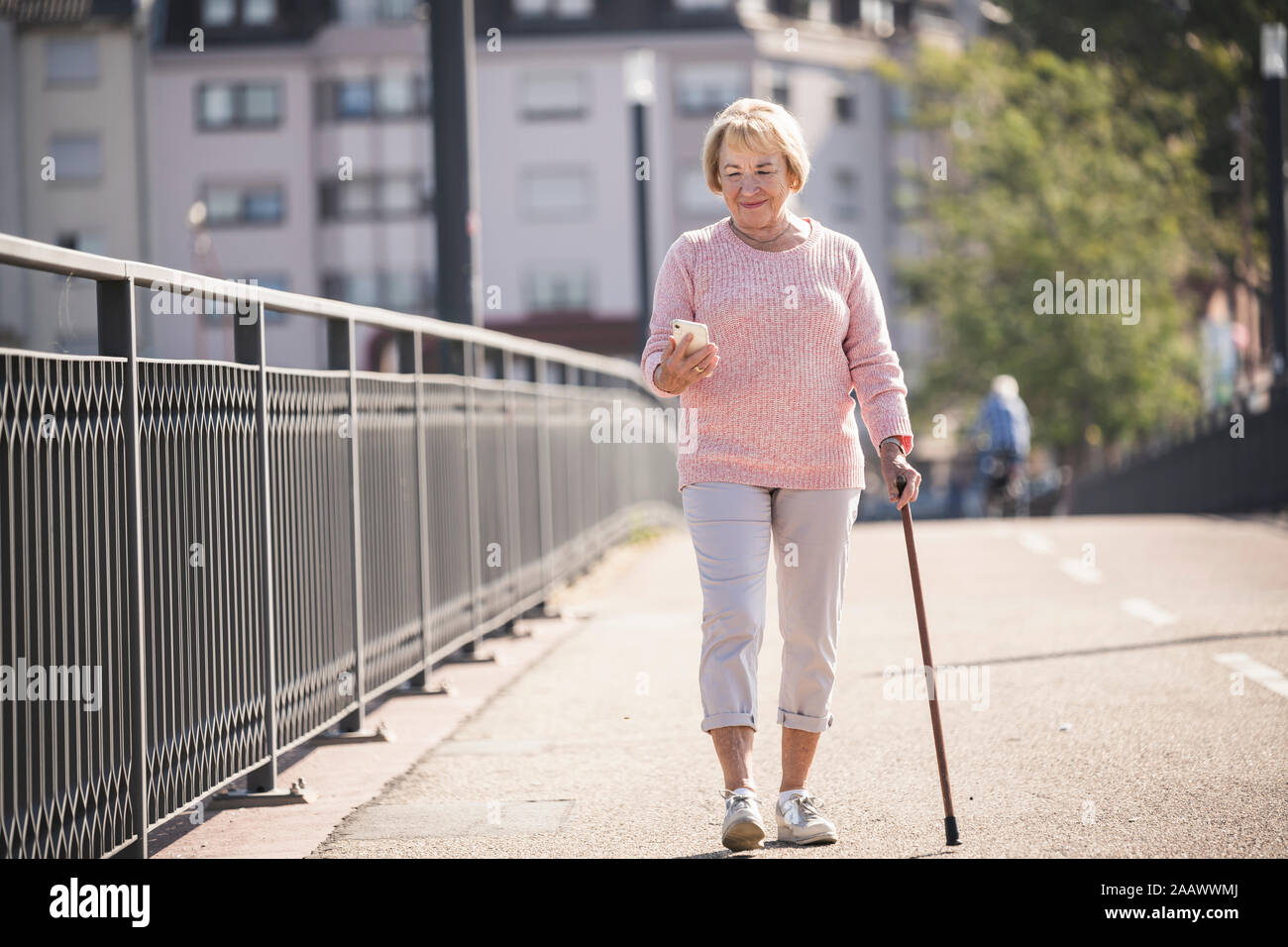 Senior woman walking on footbridge, using walking stick Stock Photo - Alamy