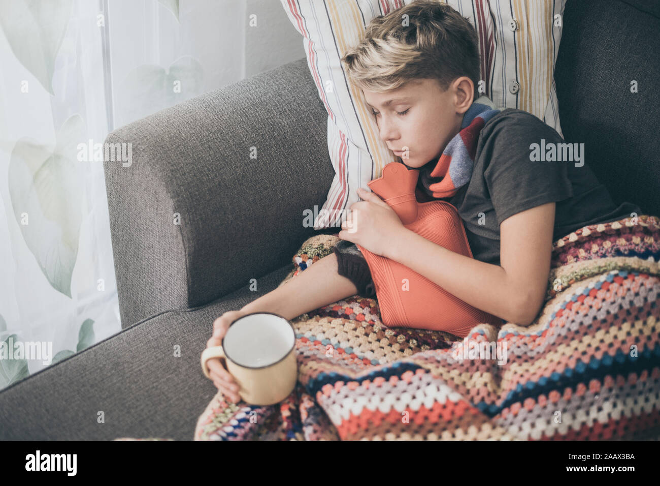 Sick boy sleeping with woolen blanket, hot water bottle and a mug. Sad ...