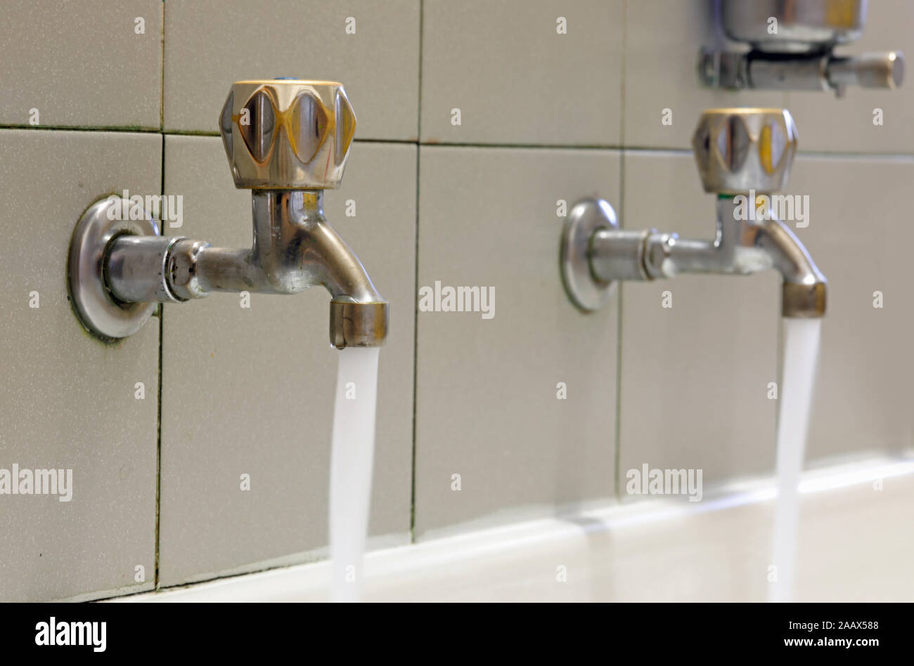 two taps with water coming out of the large sink and the soap dispenser ...