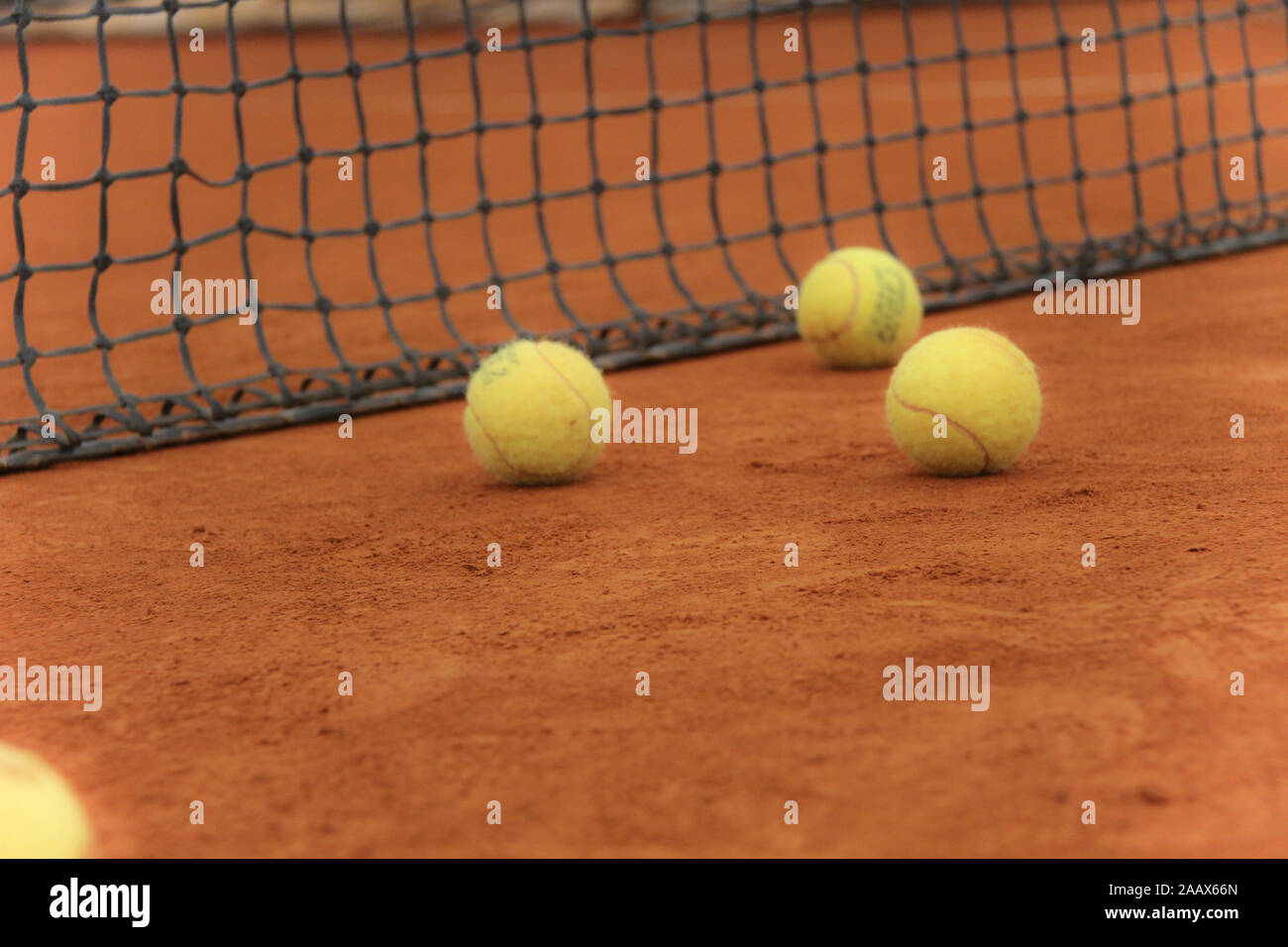 Tennis balls on red court with gray net Stock Photo - Alamy