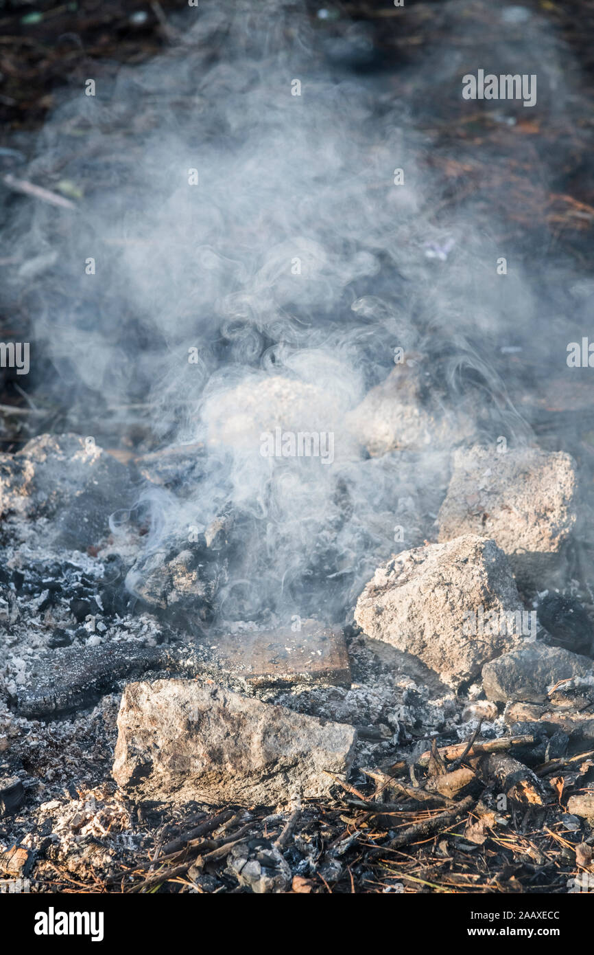 Smouldering wood ash remains from wood burning campfire set in a stone ...