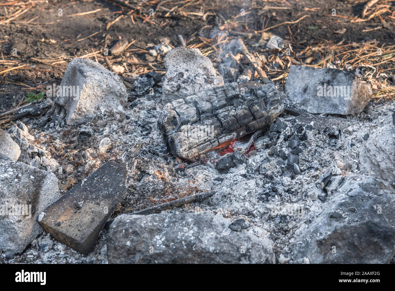 Smouldering wood ash remains from wood burning campfire set in a stone ...