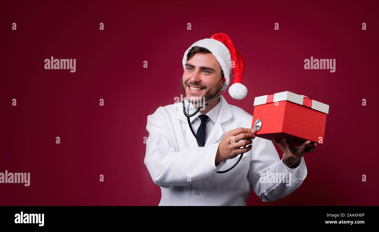 Young handsome doctor in white uniforme and Santa Claus hat standing in ...