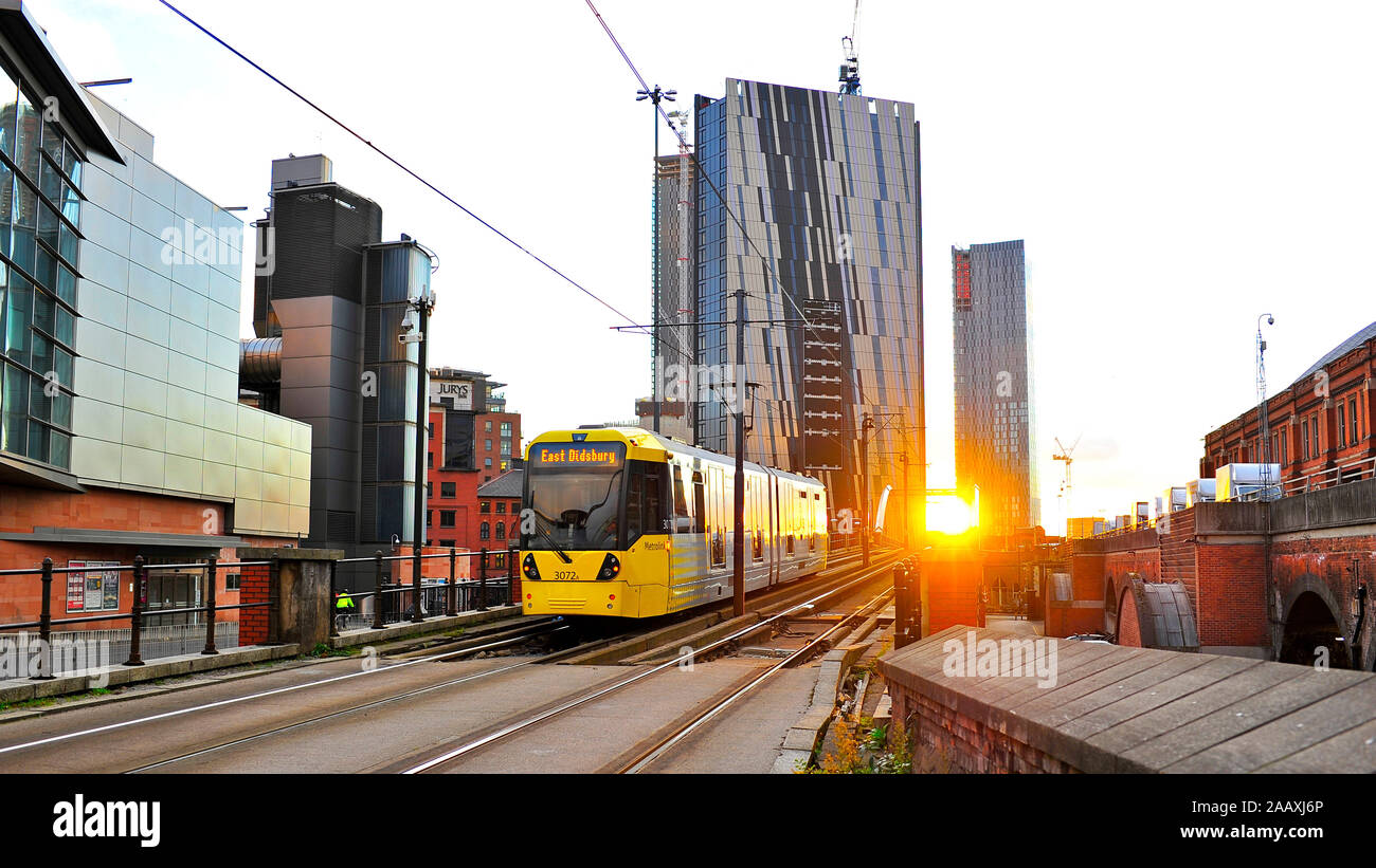 Yellow tram heads into a sun setting between buildings in Manchester ...