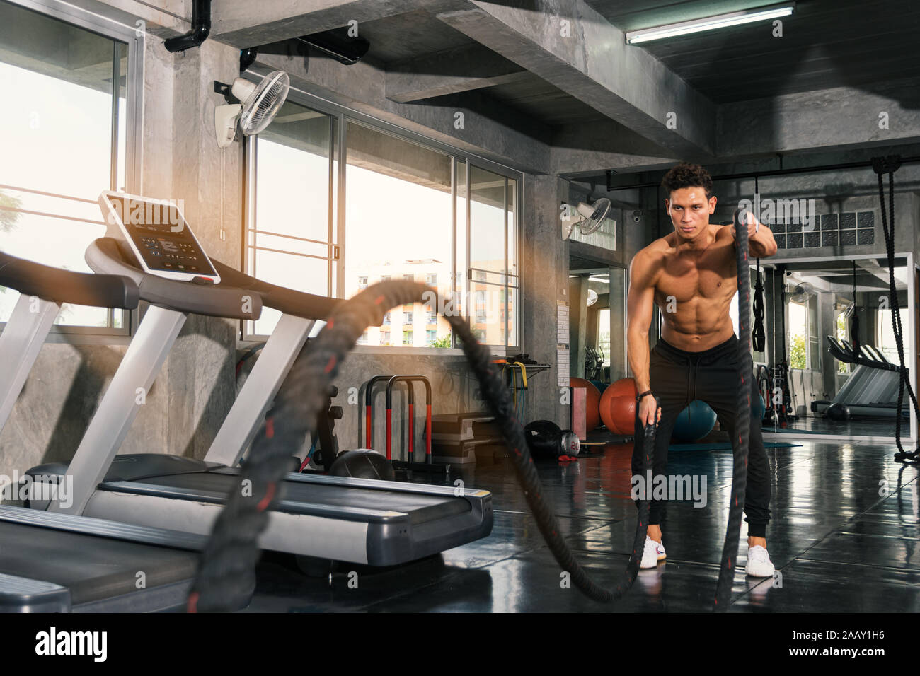 Athletic young man muscular powerful aggressive man training with rope ...