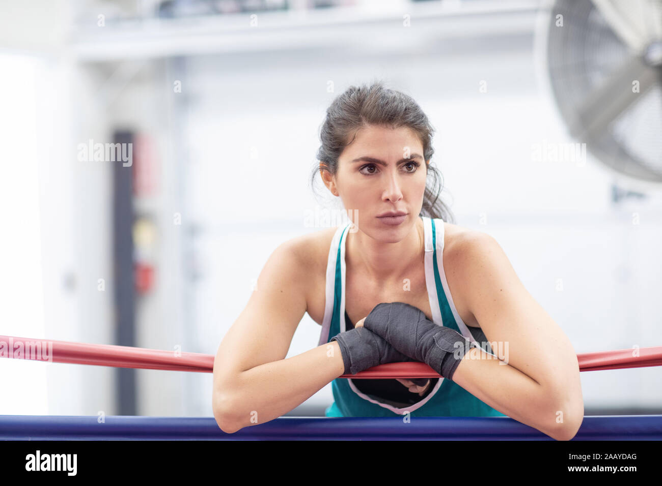 A badass female boxer is resting on ring ropes with her wraps on in a ...